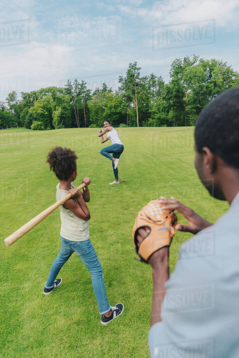 Young African American family with one child playing baseball on green ...