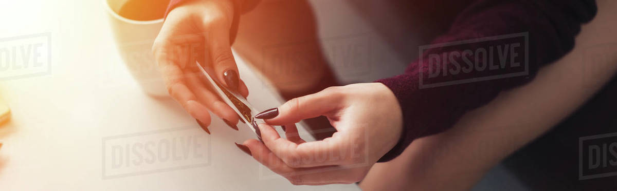 Partial view of girl sitting and rolling marijuana joint at home ...