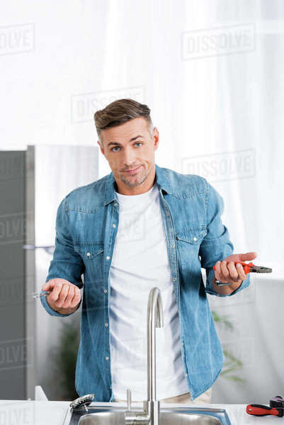 Confused man with repair tools looking at camera while standing near ...