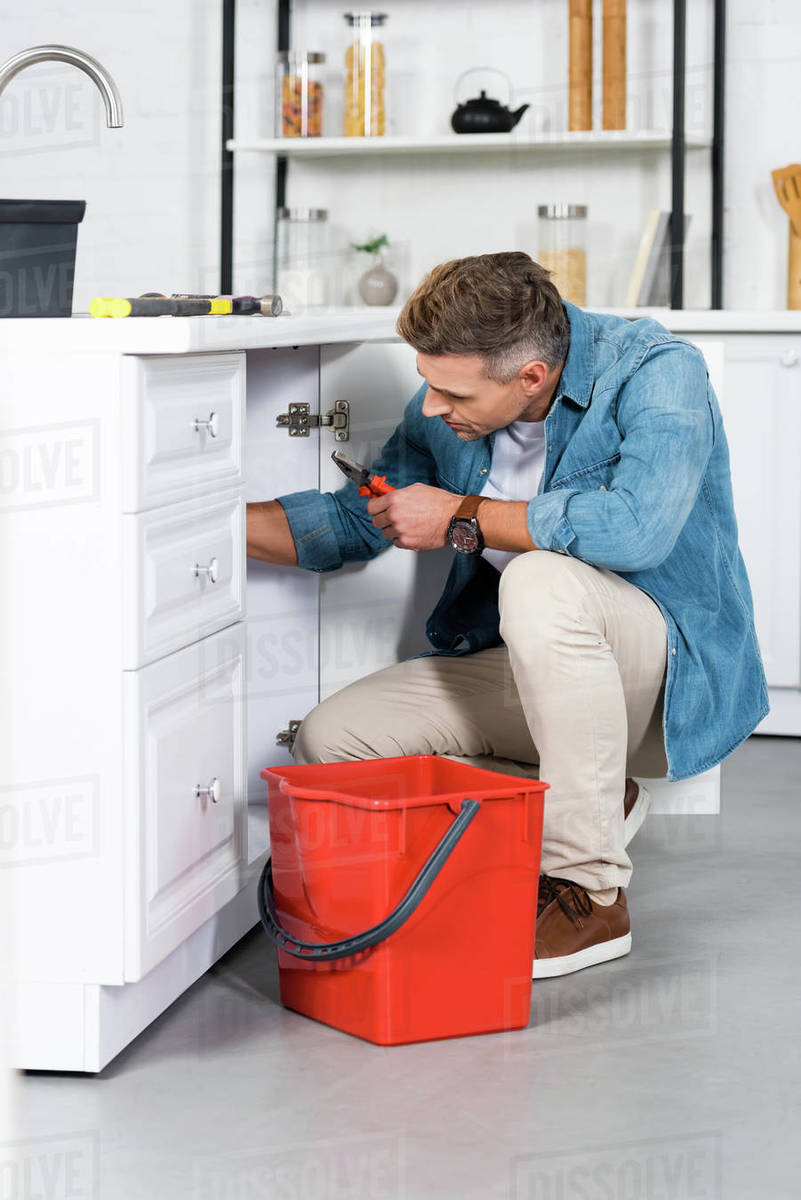 Handsome adult man repairing kitchen sink - Stock Photo - Dissolve