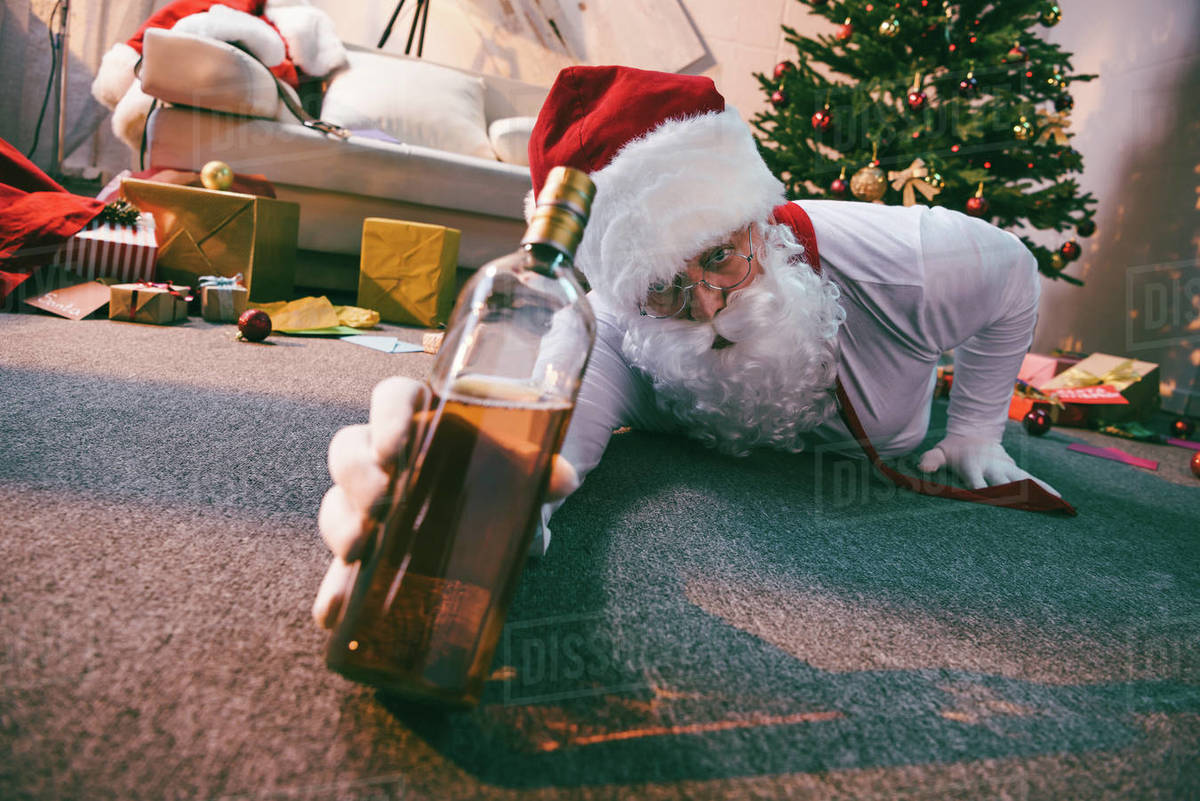 selective focus of santa claus holding bottle of whiskey while lying on ...