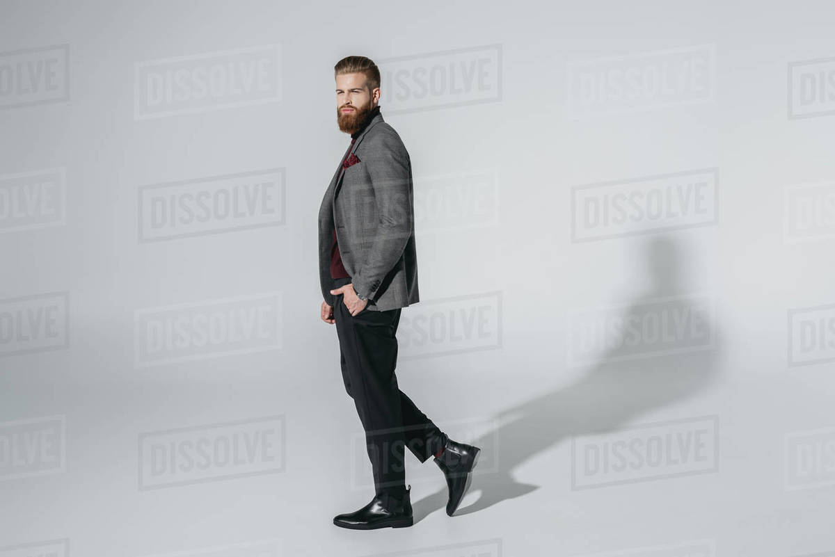 side view of attractive bearded man in stylish blazer isolated on grey ...