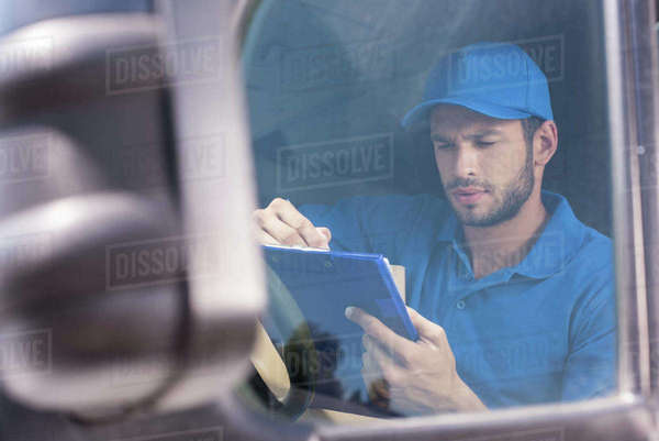 Handsome delivery man filling in documents on clipboard at car ...