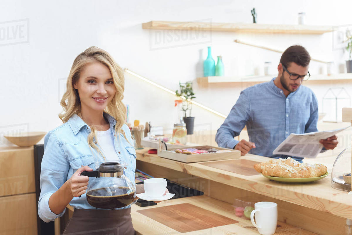 beautiful smiling young waitress holding coffee pot and cup while ...