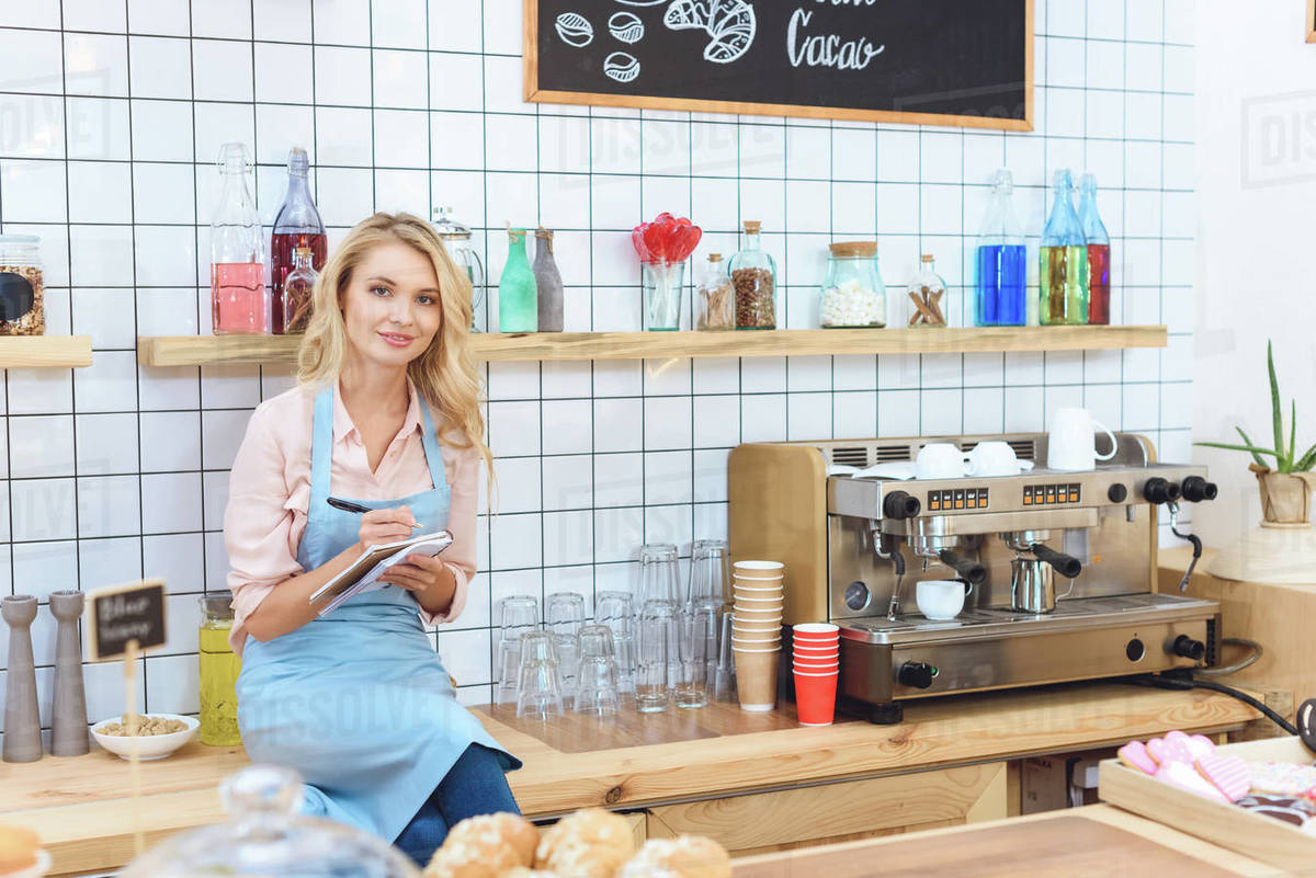 attractive young cafe owner taking notes and smiling at camera ...