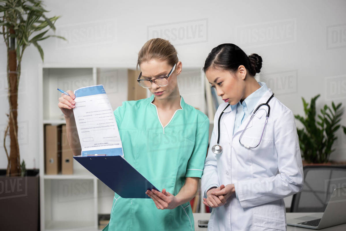 Portrait of focused doctors looking at clipboard together at clinic ...
