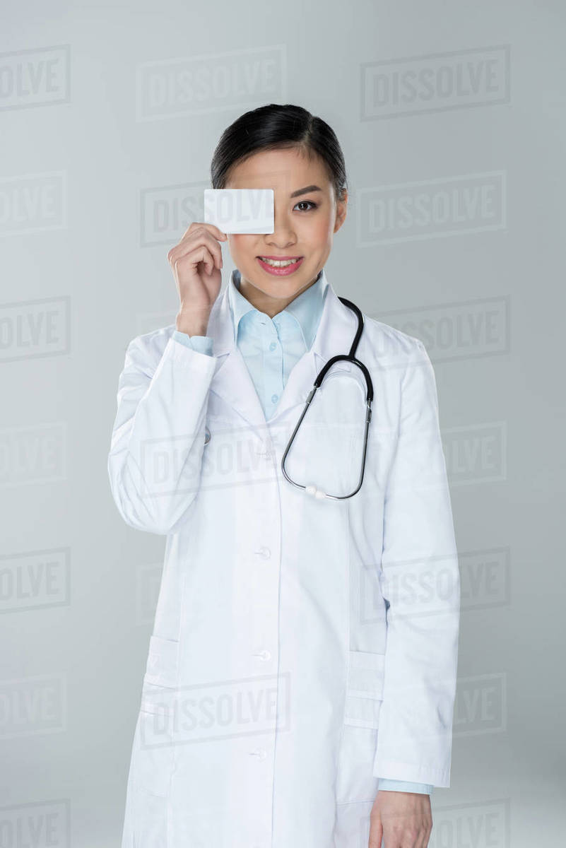 Portrait of smiling doctor covering eye with blank card in hand ...
