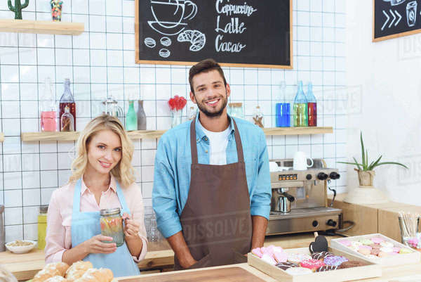 Cheerful young cafe workers in aprons smiling at camera - Royalty-free ...