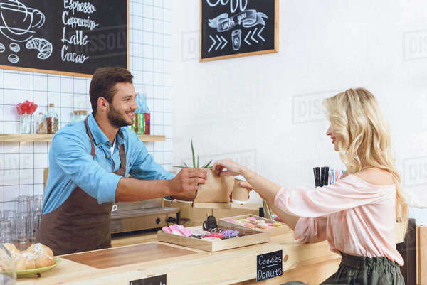 Handsome young waiter giving take away food and coffee in paper cup to ...