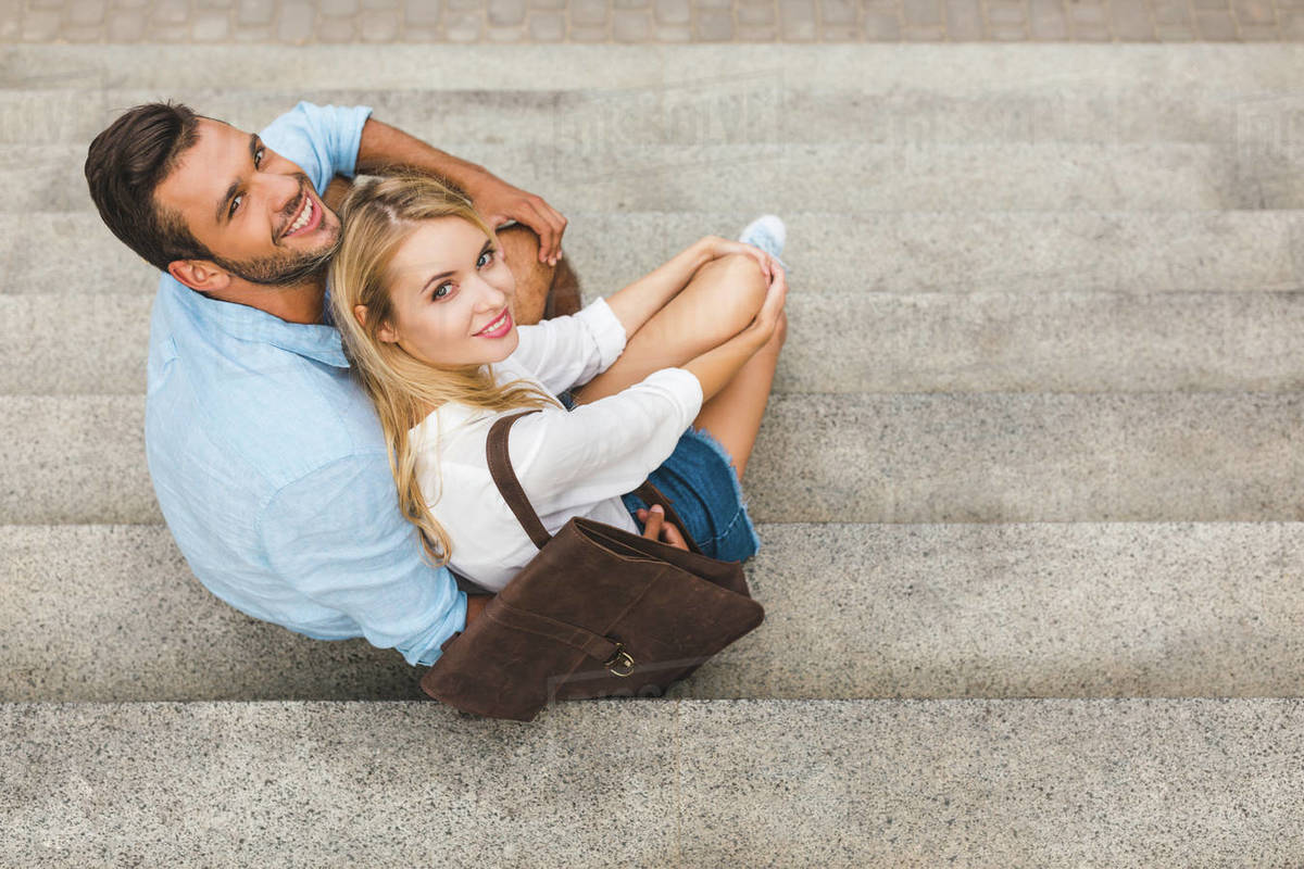 Overhead view of cheerful couple looking at camera while sitting on ...