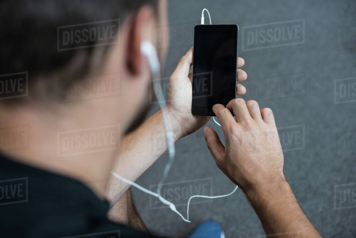 Cropped shot of young man in earbuds using his smartphone - Royalty ...