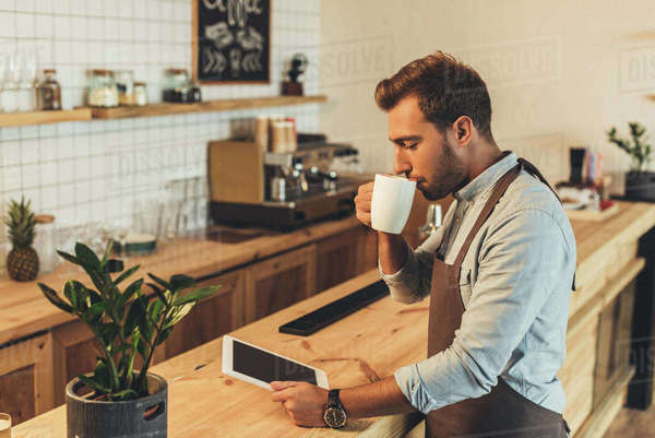 Side view of barista drinking aromatic coffee while using tablet in ...