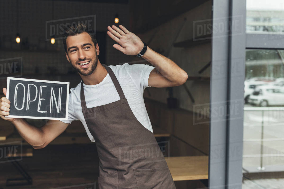 Portrait of smiling waiter waving to someone while holding chalkboard ...