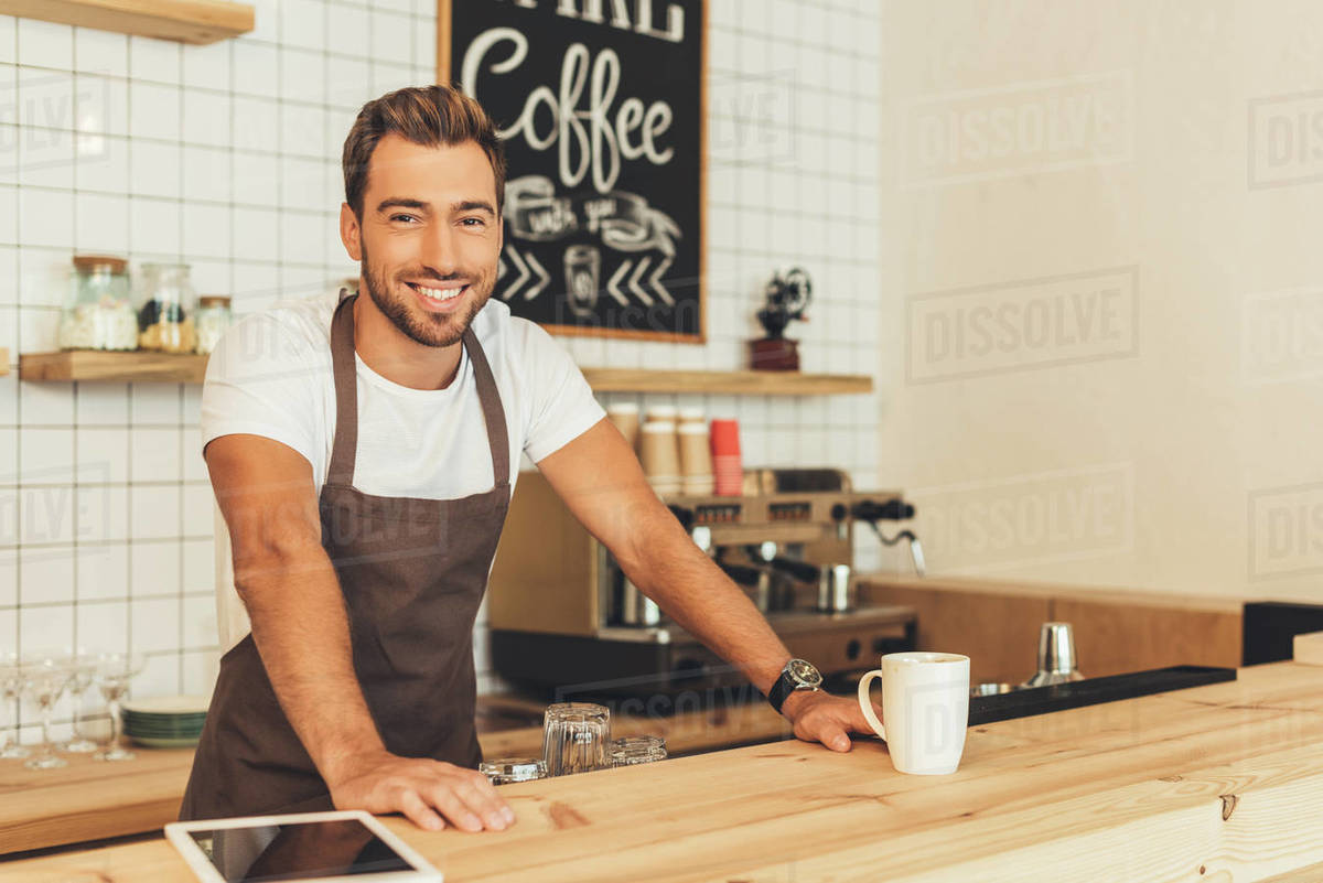Portrait of smiling barista leaning on counter in coffee shop - Royalty ...