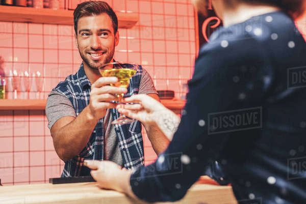 Portrait of smiling young barman giving alcohol cocktail to woman in ...