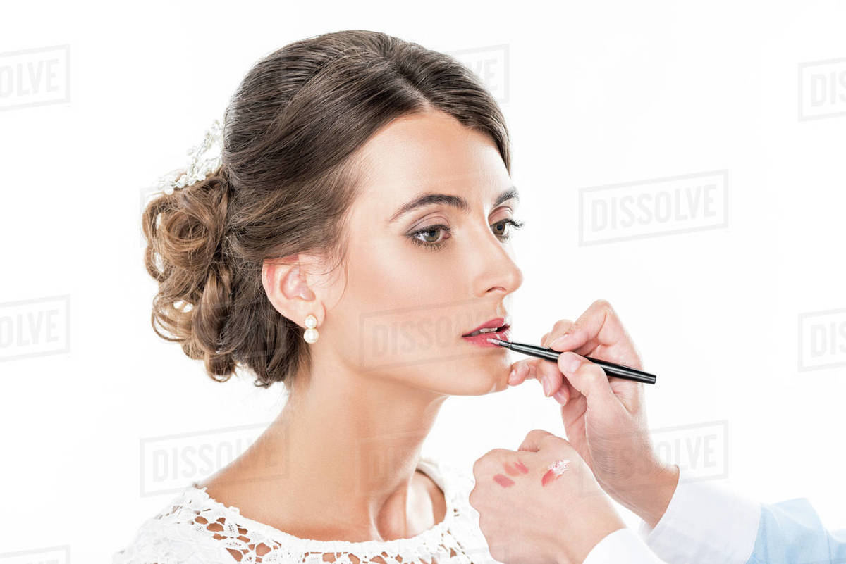 Side view of makeup artist applying lipstick on models lips using lip ...