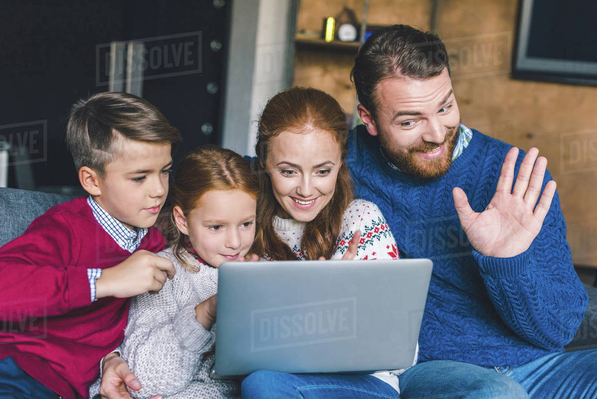Funny young family making video call with laptop - Stock Photo - Dissolve