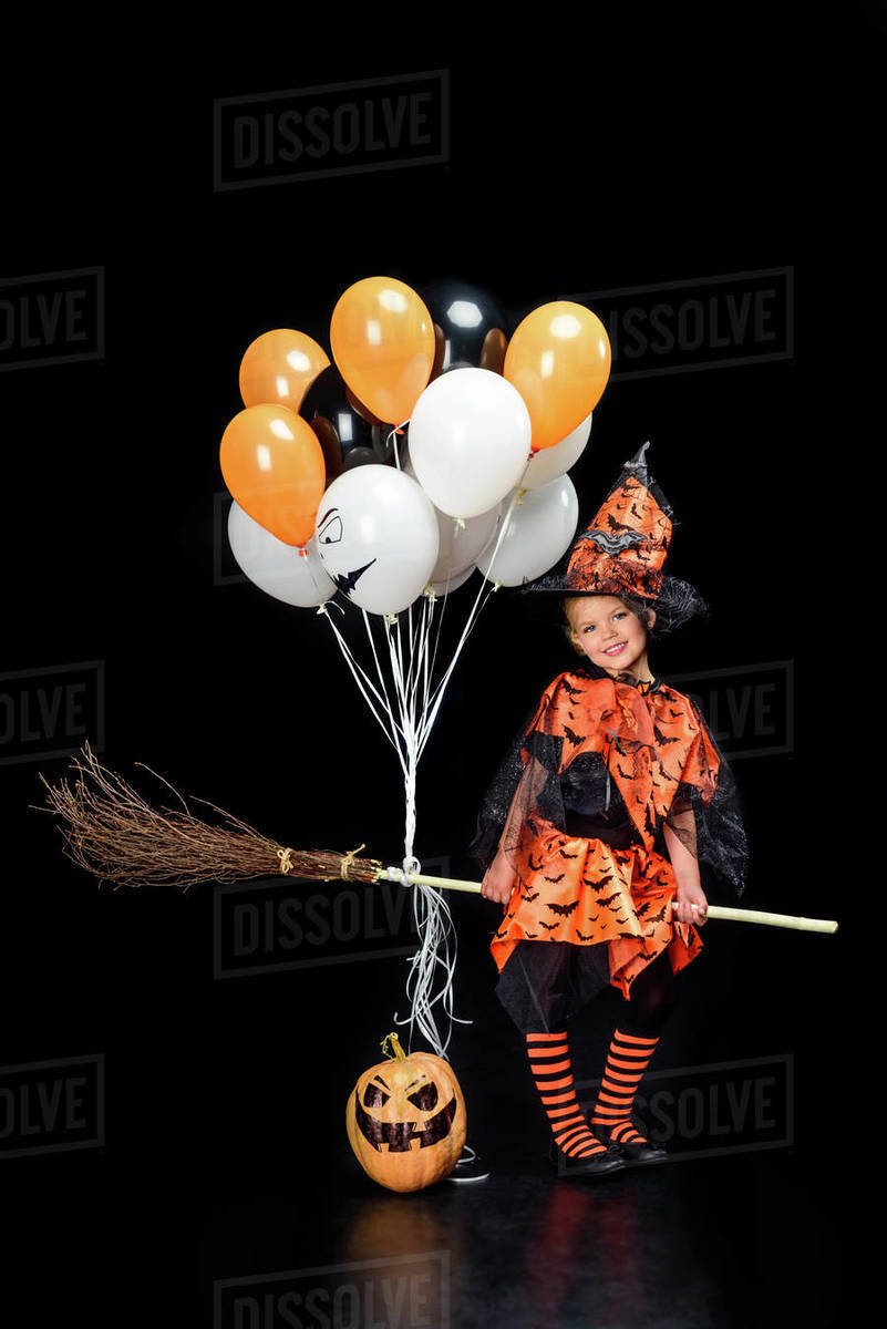Kid in Halloween costume of witch with broom, balloons and jack o ...