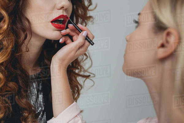 cropped view of attractive model and makeup artist applying lipstick in ...