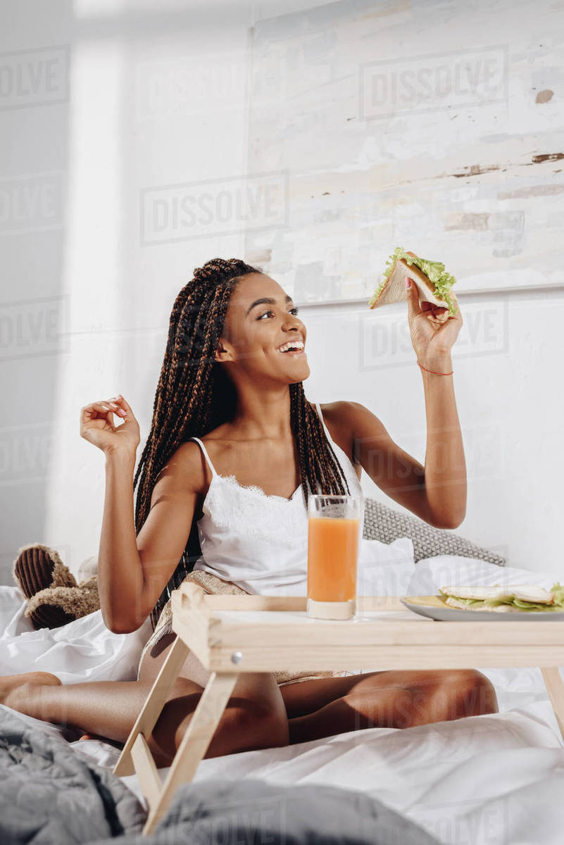 Happy African American woman eating breakfast in bed - Royalty-free ...