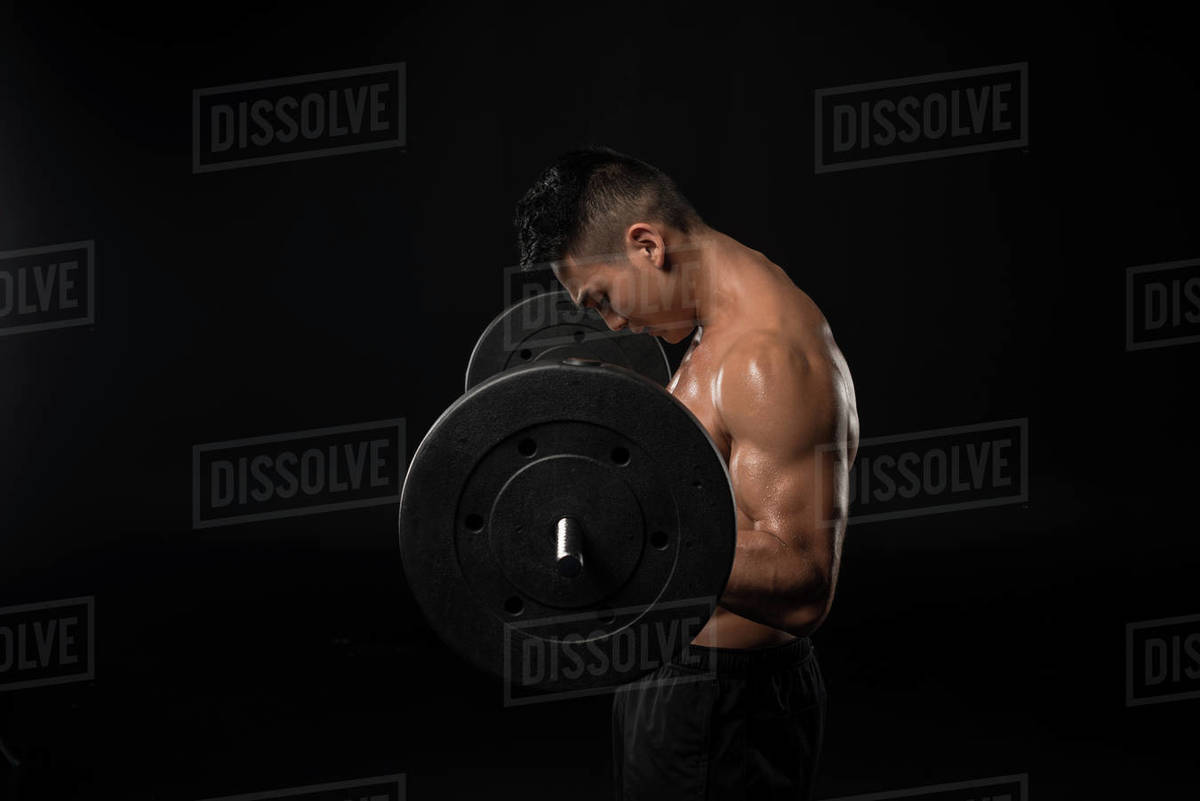 Side view of muscular Asian man lifting barbell isolated on black ...