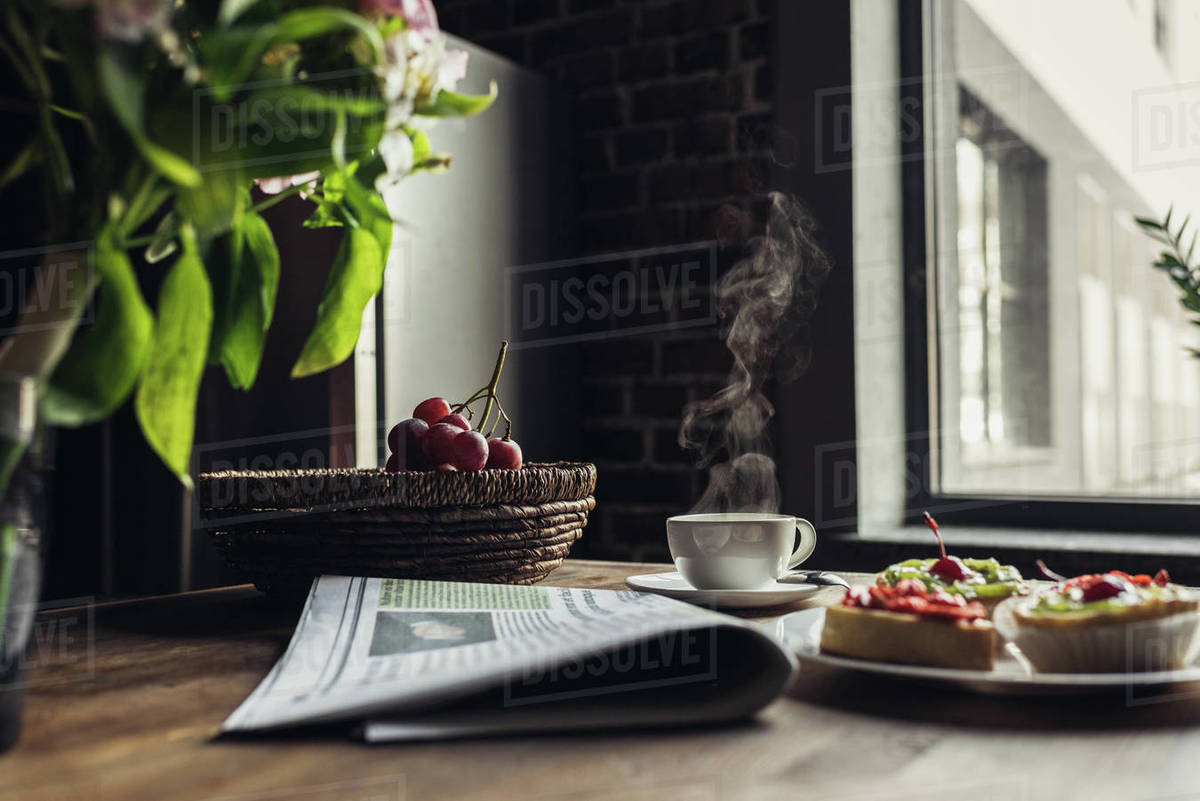 Still life of newspaper, breakfast with cakes and hot coffee on kitchen ...
