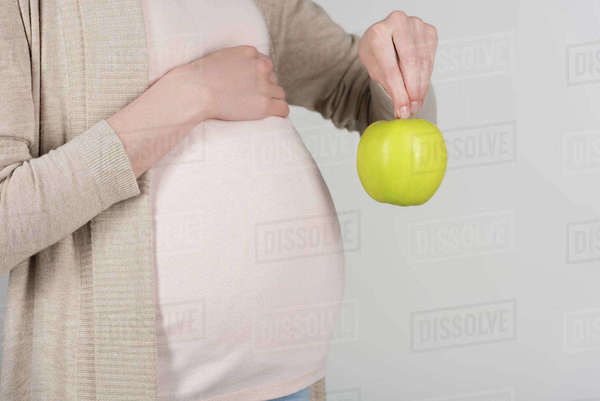 Close-up, cropped image of pregnant woman's belly and apple in hands ...