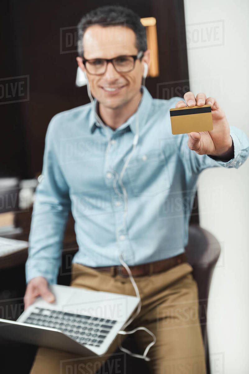 Businessman showing his credit card to camera while holding laptop ...