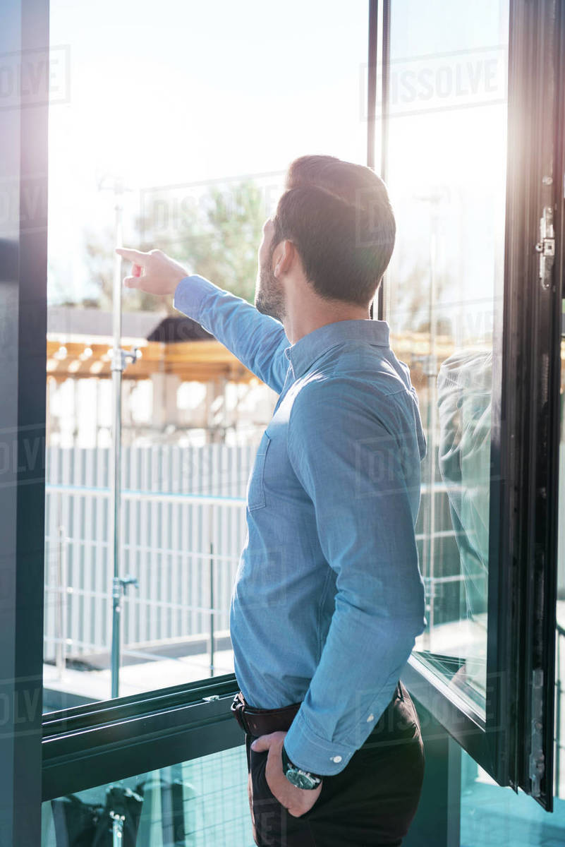 Back view of young businessman pointing at window in office - Stock ...