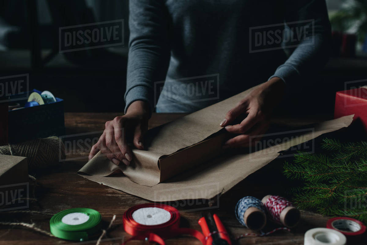 Cropped shot of woman wrapping book in craft paper as christmas gift ...