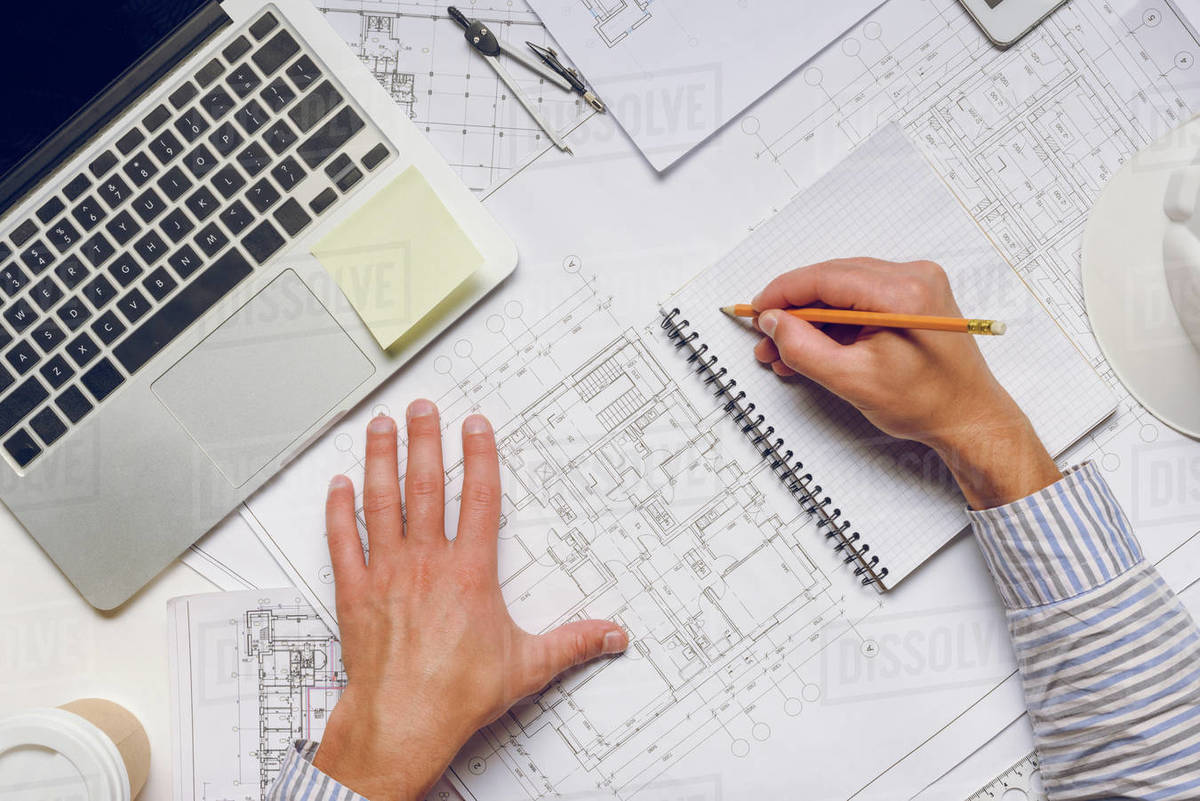 cropped shot of architect writing in notebook while working on ...