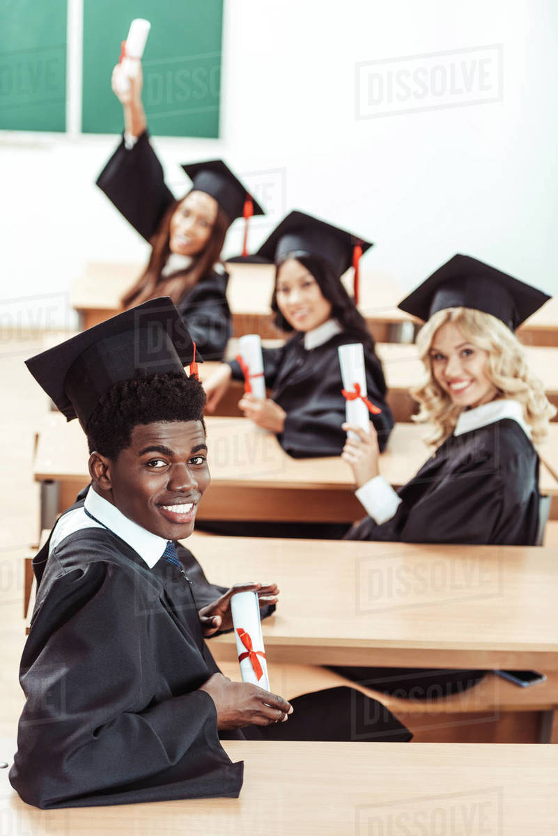 young multiethnic students in graduation costumes sitting in class ...
