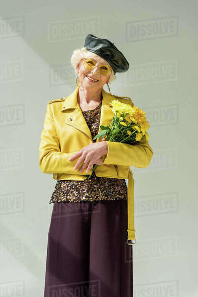 stylish senior woman in yellow leather jacket with bouquet of yellow ...