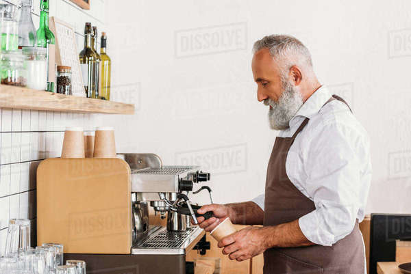 Side view of focused senior barista using coffee machine while making ...