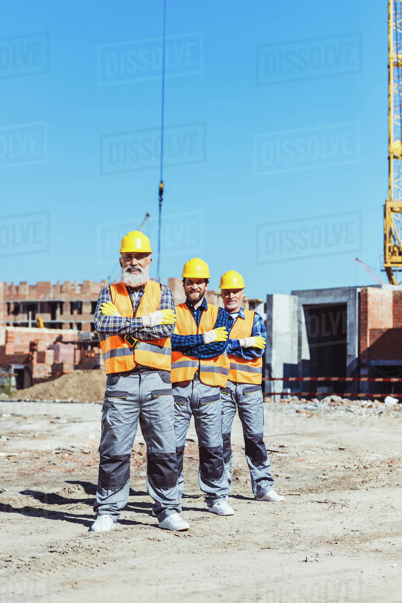 Three labour workers posing with arms crossed at the construction site ...