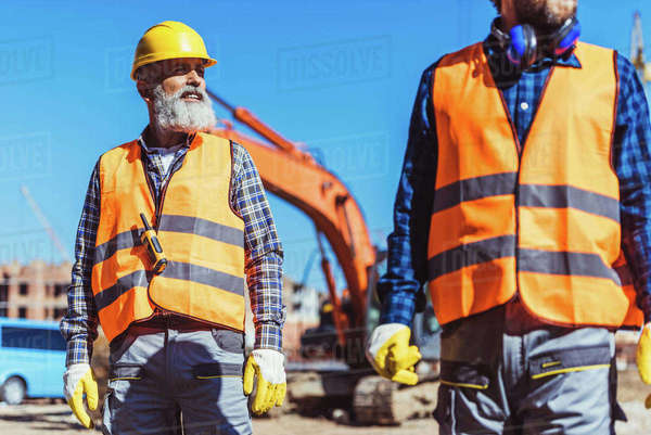 Two workers in reflective vests and hardhats standing at construction ...
