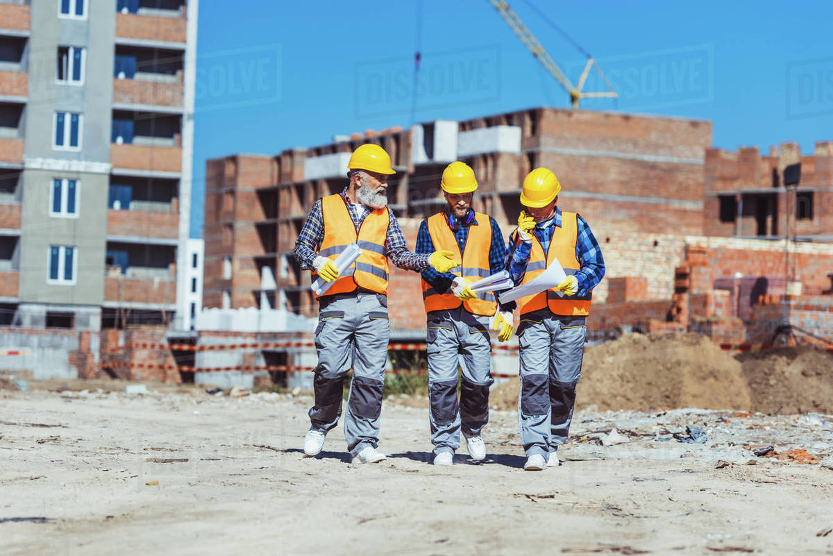 Three workers in reflective vests and hardhats walking together across ...