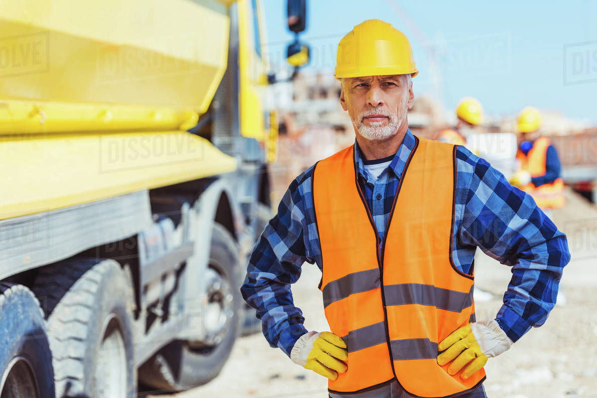 Worker in reflective vest and hardhat standing with hands on waist at ...