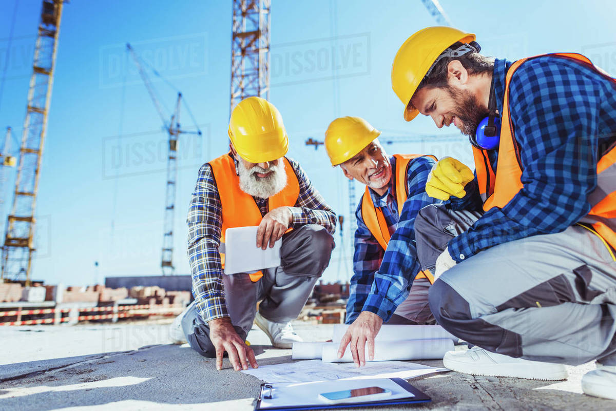 Three construction workers sitting on concrete at construction site ...