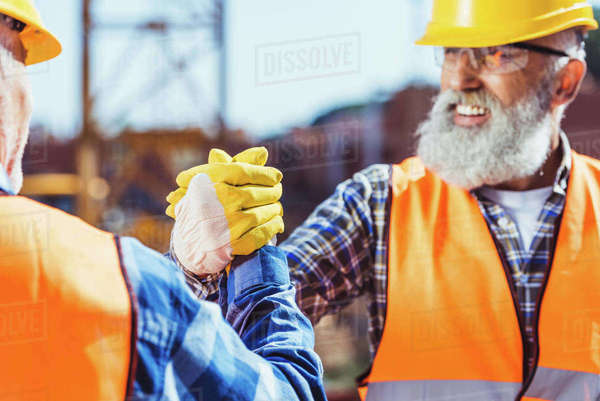 Smiling construction worker in protective uniform shaking hands with ...