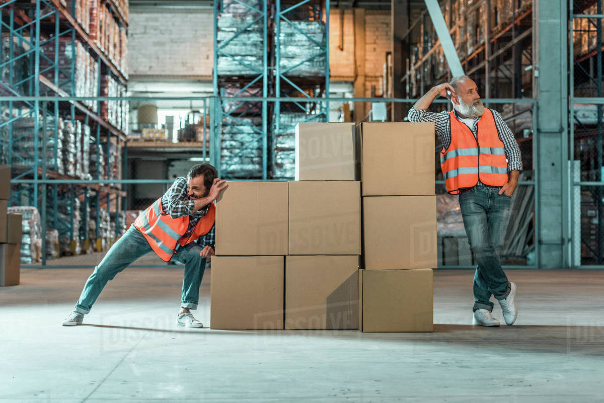 Full length view of two male workers in vests working with boxes in ...