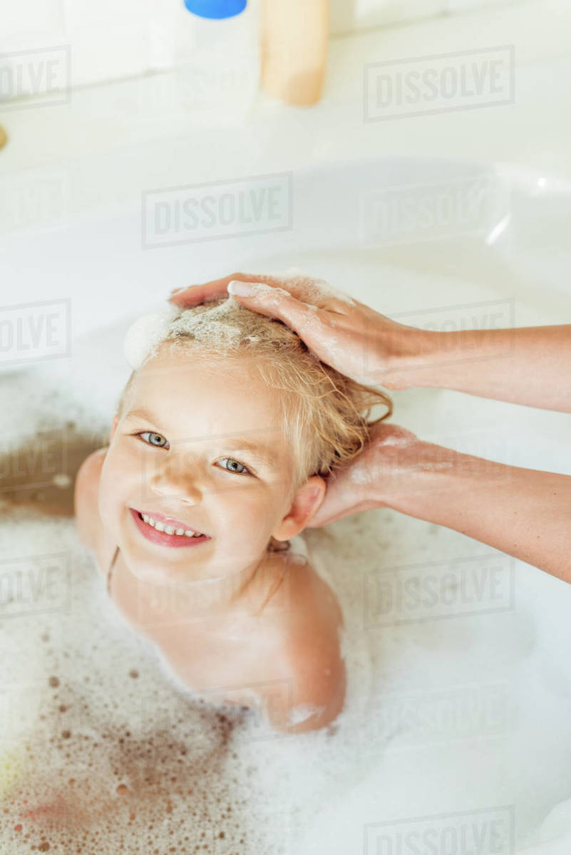 Cropped shot of mother washing adorable little daughter in bathtub ...