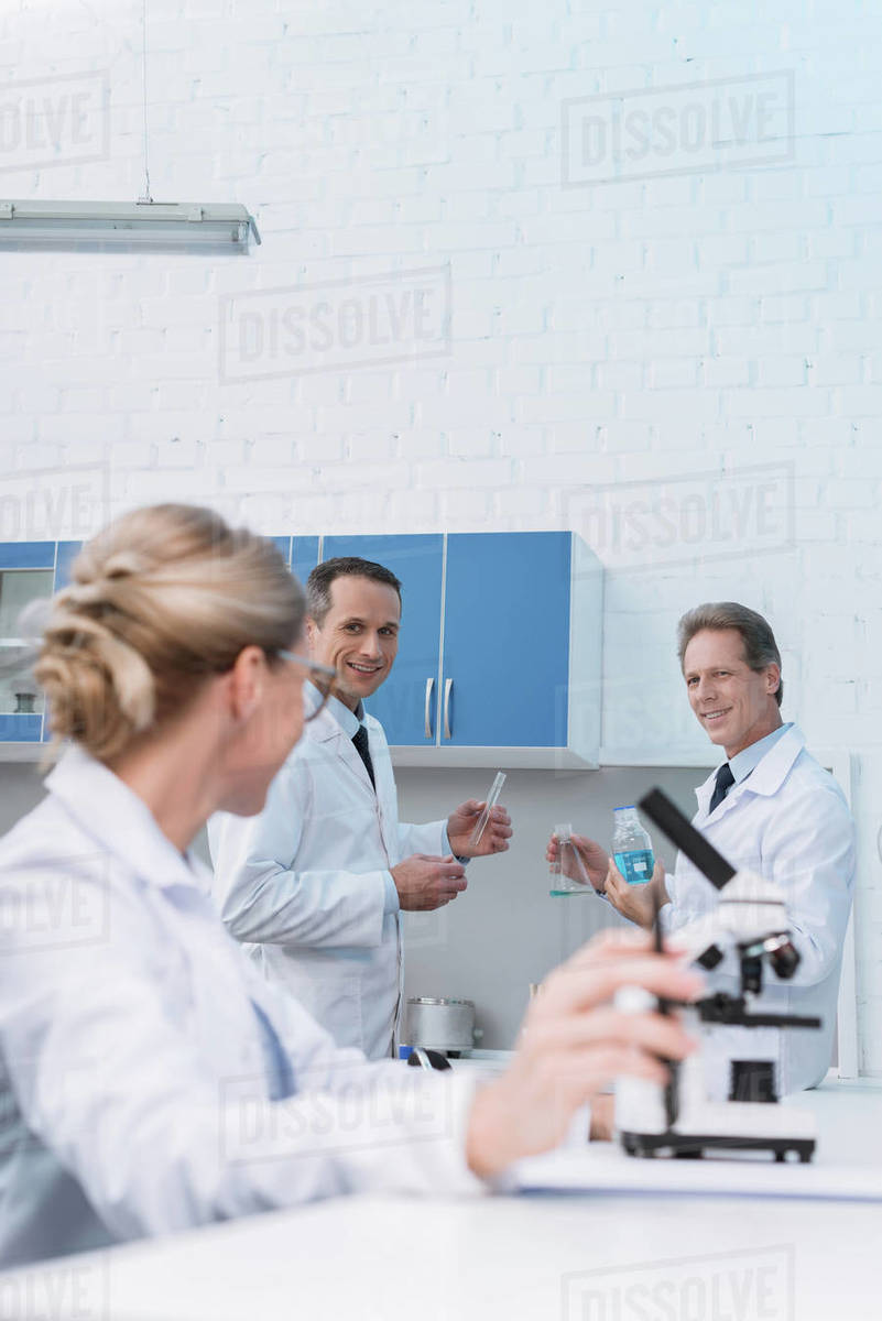 Smiling chemists doing experiments with reagents and discussing work in ...