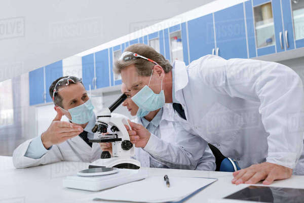 Doctors in lab coats and sterile masks, doing microscope sample ...