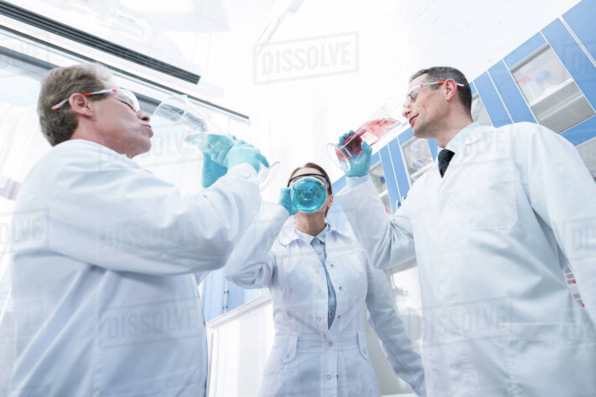 A team of doctors in lab coats pretending to drink from test tubes in ...