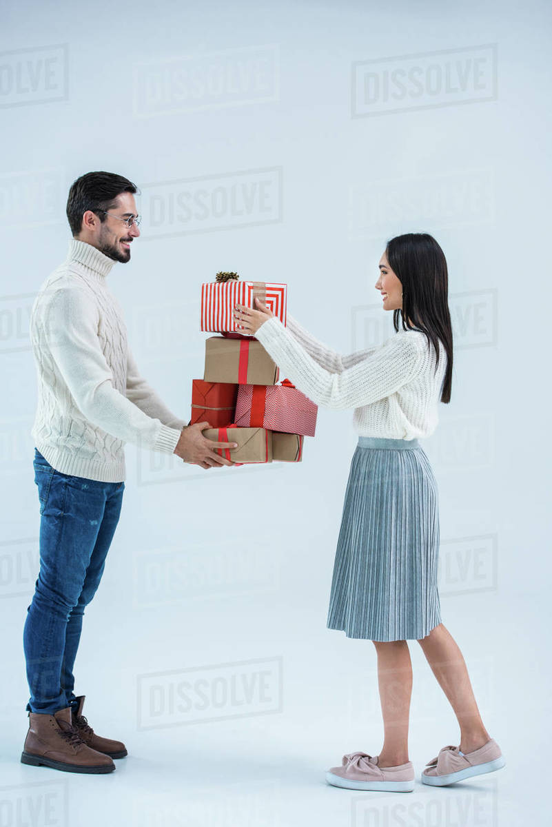 Side view of smiling multicultural couple holding stack of wrapped ...