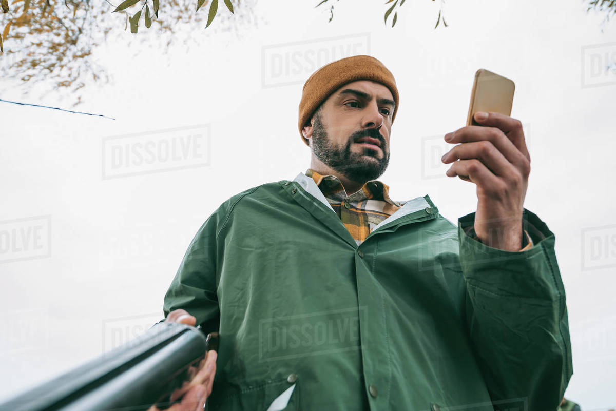 Bottom view of handsome hunter standing with a gun and looking at ...