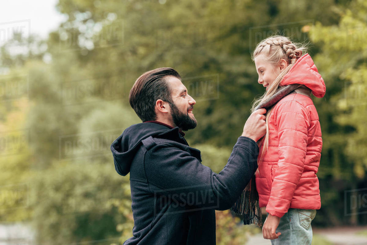 side view of happy father and daughter looking at each other in autumn ...