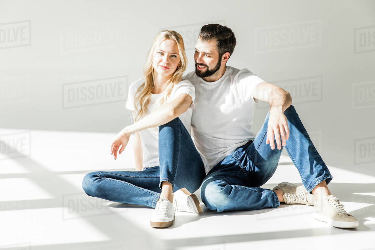 Beautiful happy young couple sitting together in studio on grey ...