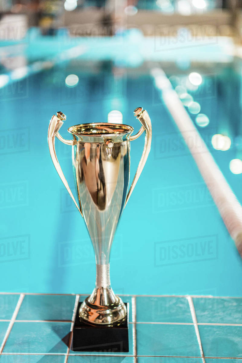 Golden trophy cup at competition swimming pool - Stock Photo - Dissolve
